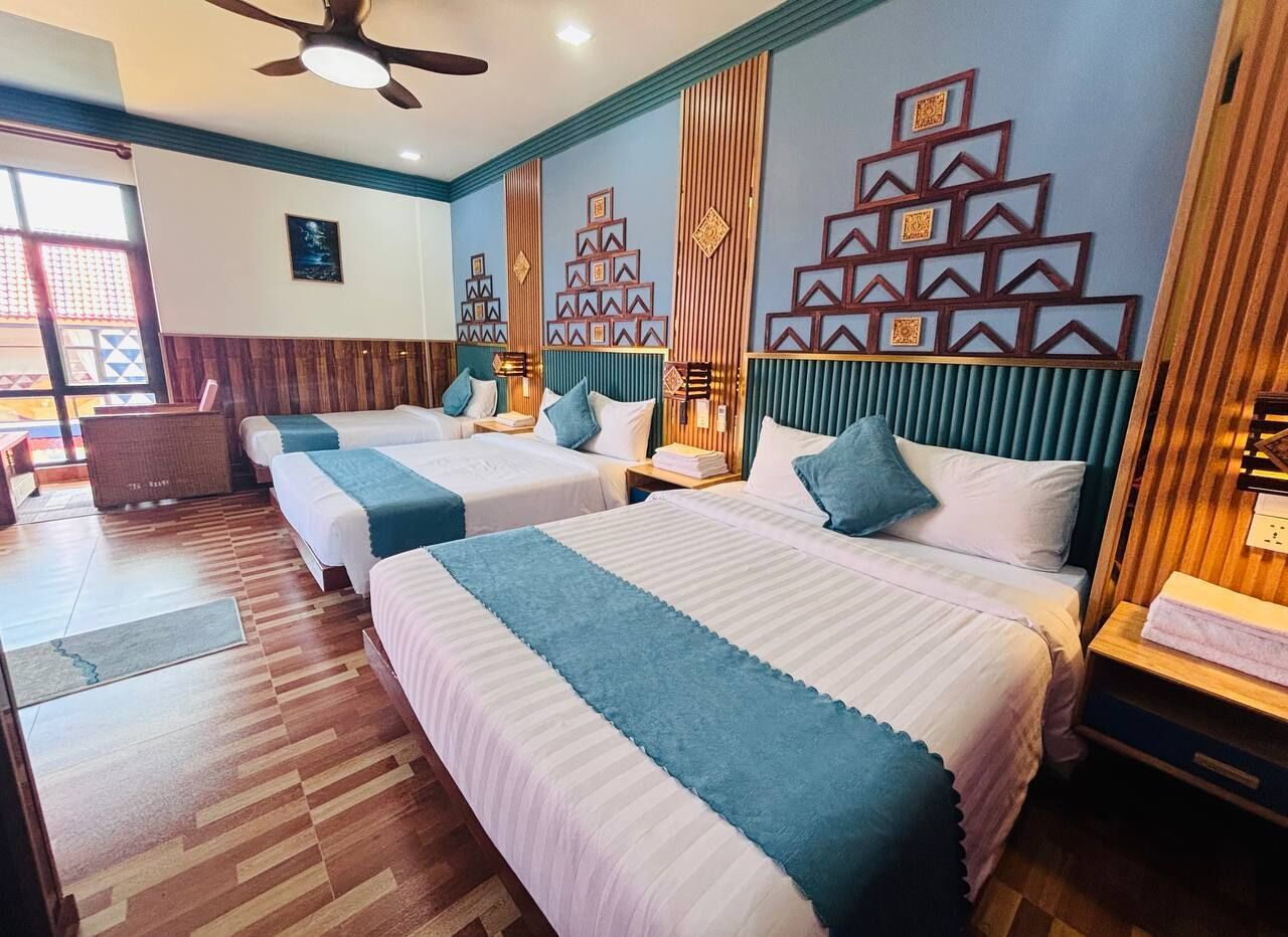 Quarto de hotel com duas camas, piso de madeira, ventoinha no teto e painéis decorativos na parede.