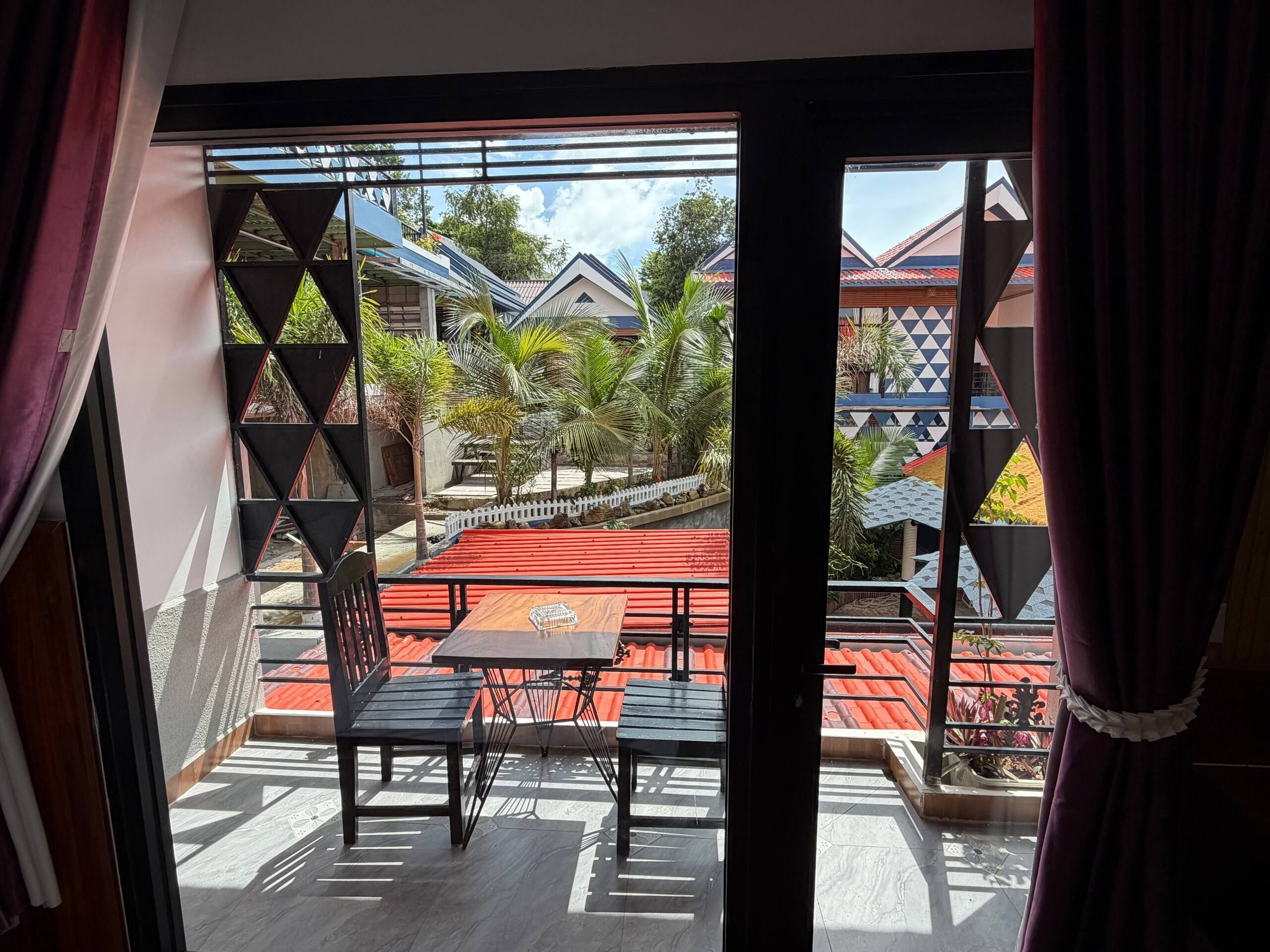 A balcony with a table and chairs, a view of a residential area with houses and palm trees.