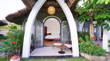 Uma villa moderna com telhado de colmo, um quarto com cama e área de estar, e um jardim com vasos de plantas e flores.