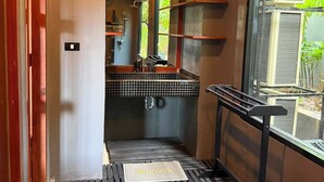 Um corredor estreito com piso de grade de metal preto, uma janela com tela de metal e um revestimento de azulejos ao fundo.