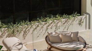 Uma área ao lado da piscina com uma espreguiçadeira, um espaço de estar acolchoado e uma piscina transparente.