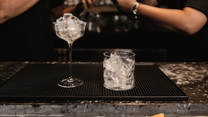 Um bar com dois bartenders, uma taça de martini e um copo com cubos de gelo.