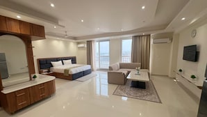 Quarto de hotel moderno com cama, sofá, mesa de centro e um espelho grande.