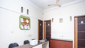Um quarto com escrivaninha, cadeiras, ventilador de teto e um quadro de avisos.