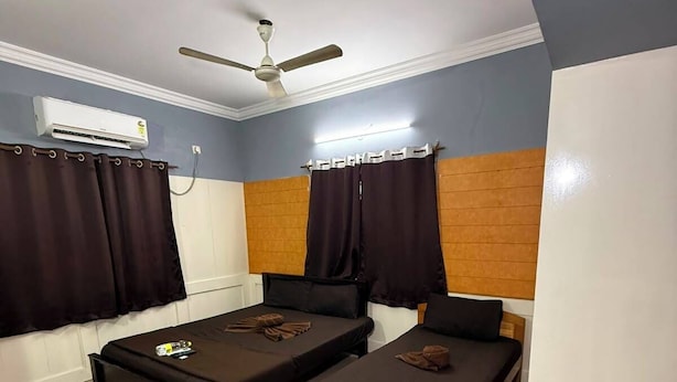 Quarto com duas camas, ar-condicionado, ventilador de teto e janela com cortinas.
