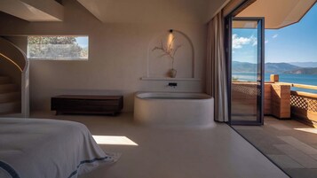 Quarto moderno com uma cama grande, banheira integrada e vista para o mar.