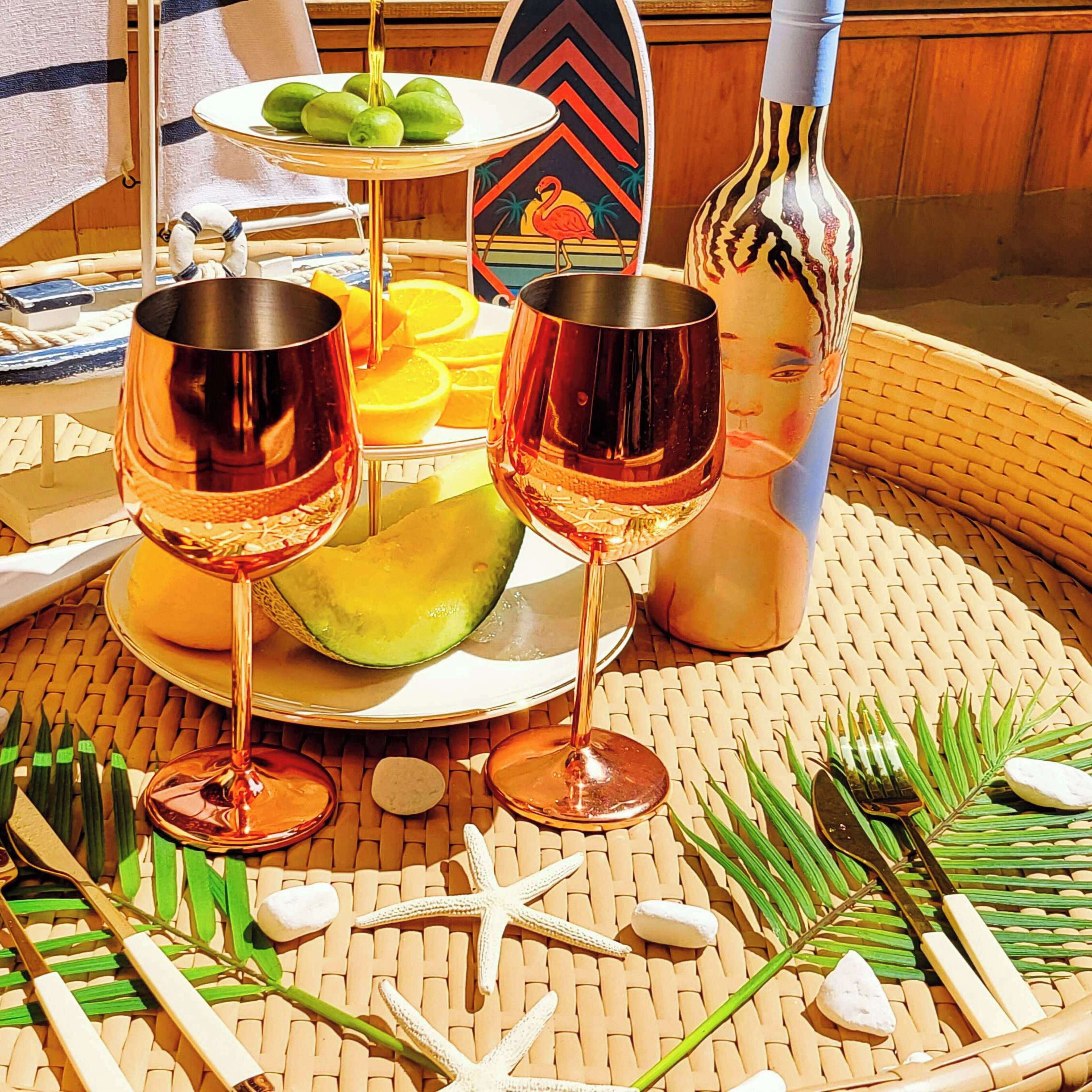 Disposição de mesa com tema tropical, dois copos, um prato com frutas e uma garrafa decorativa.