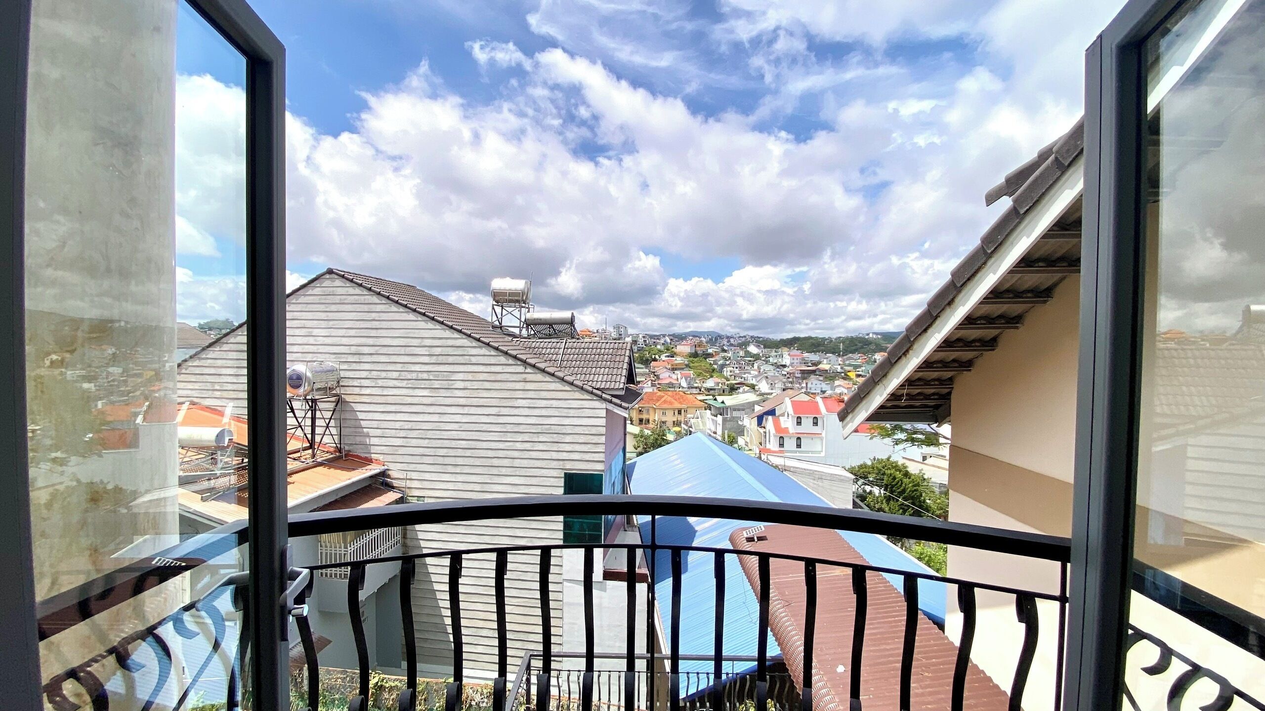 Varanda com guarda-corrimão de metal, vista para área residencial com vários edifícios e céu claro.