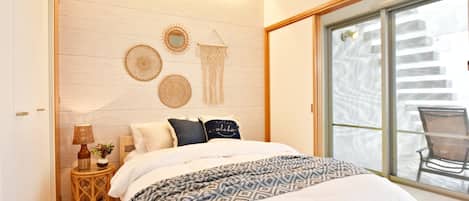 Quarto com cama, mesa de cabeceira, decoração na parede e vista através de uma porta de correr de vidro.
