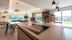 Uma cozinha moderna com uma ilha central, iluminação pendente e grandes janelas com vista para o exterior.