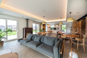 Uma sala de estar moderna com um sofá cinzento, área de jantar com mobiliário de madeira e cozinha com iluminação pendente.