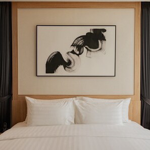 Quarto de hotel com uma cama, cabeceira e uma obra de arte emoldurada na parede.