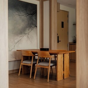 Uma área de refeições com uma mesa e cadeiras de madeira, um quadro abstrato grande na parede e uma porta de madeira ao fundo.