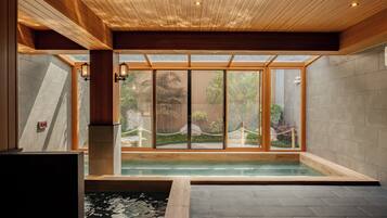 Uma área interna de piscina moderna, com teto de madeira, paredes de pedra e vista para um jardim.