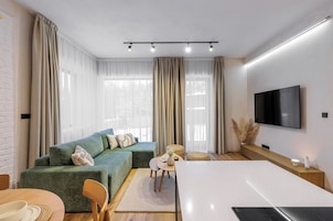 Uma sala de estar moderna com um sofá verde, uma mesa de jantar e uma televisão de tela plana na parede.
