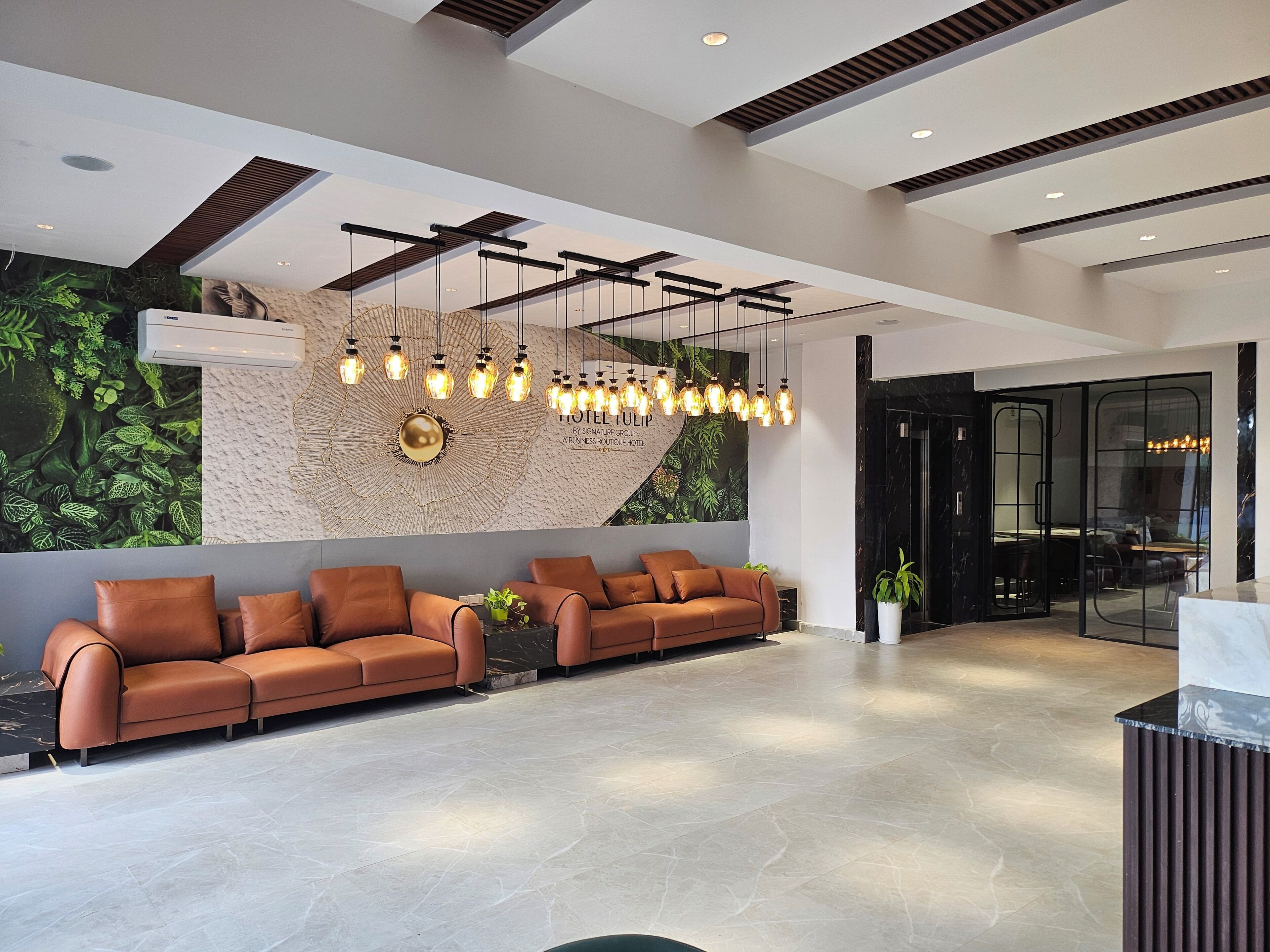 Um hall de hotel moderno com um sofá modular, iluminação pendente, um mural e um balcão de recepção.