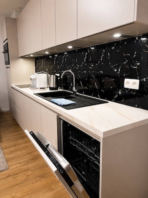 Cozinha moderna com painel de fundo de mármore preto, eletrodomésticos de aço inoxidável e lava-louças integrada aos armários.