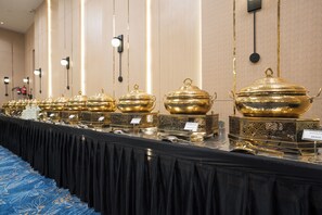 Uma mesa comprida com vários utensílios dourados para servir e recipientes, provavelmente para um buffet ou serviço de catering.