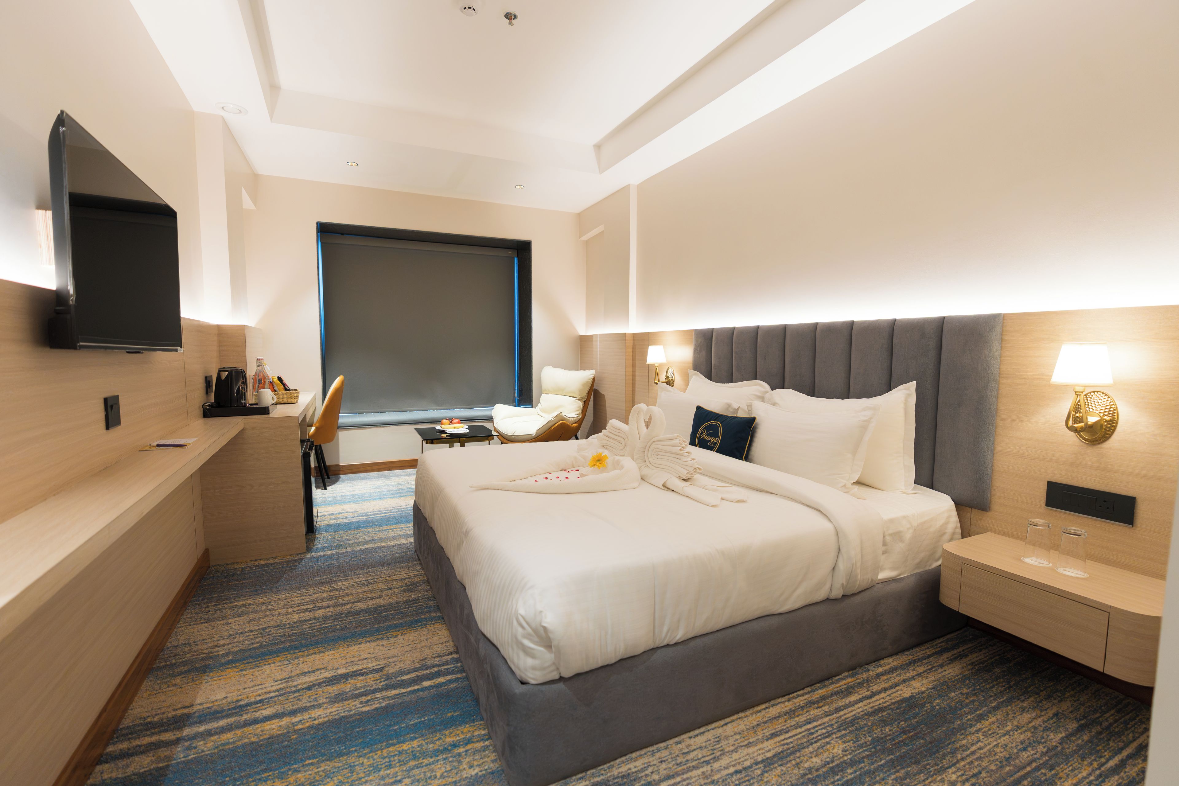 Quarto de hotel com uma cama grande, uma escrivaninha, uma cadeira, uma televisão e uma janela.