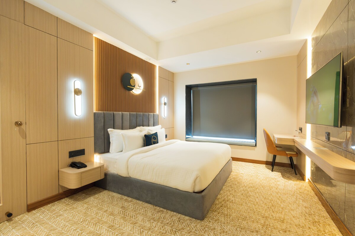 Quarto de hotel moderno com uma cama grande, uma escrivaninha e uma TV.