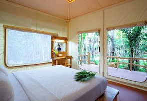 Quarto com cama, escrivaninha e amplas janelas com vista para um jardim.