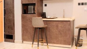 Uma cozinha moderna com armários escuros, micro-ondas e espaço para bar. Há uma mesa de jantar com controle remoto e objetos decorativos.