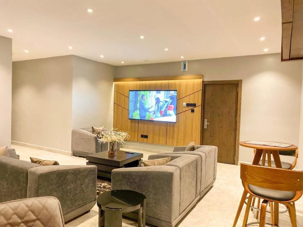 Uma sala de estar moderna com televisão de tela plana presa a uma parede de madeira, sofás cinzas, uma mesa de centro e uma cadeira de madeira.