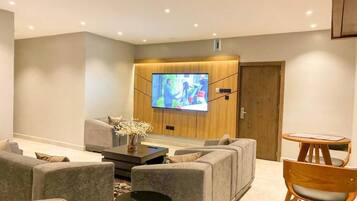 Uma sala de estar moderna com televisão de tela plana presa a uma parede de madeira, sofás cinzas, uma mesa de centro e uma cadeira de madeira.
