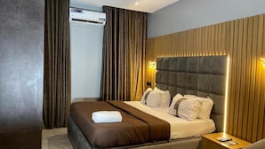 Quarto de hotel moderno com uma cama grande, cabeceira de madeira, mesa de cabeceira e unidade de ar condicionado fixada na parede.