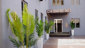 Edifício moderno com entrada central, plantas em vasos e teto trabalhado.