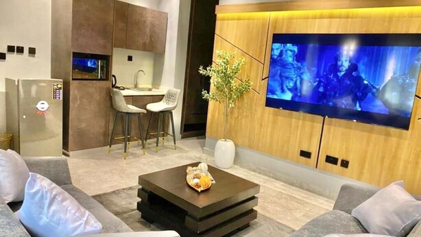 Uma sala de estar moderna com uma TV de tela plana, uma mesa de centro e uma área de jantar com cadeiras.