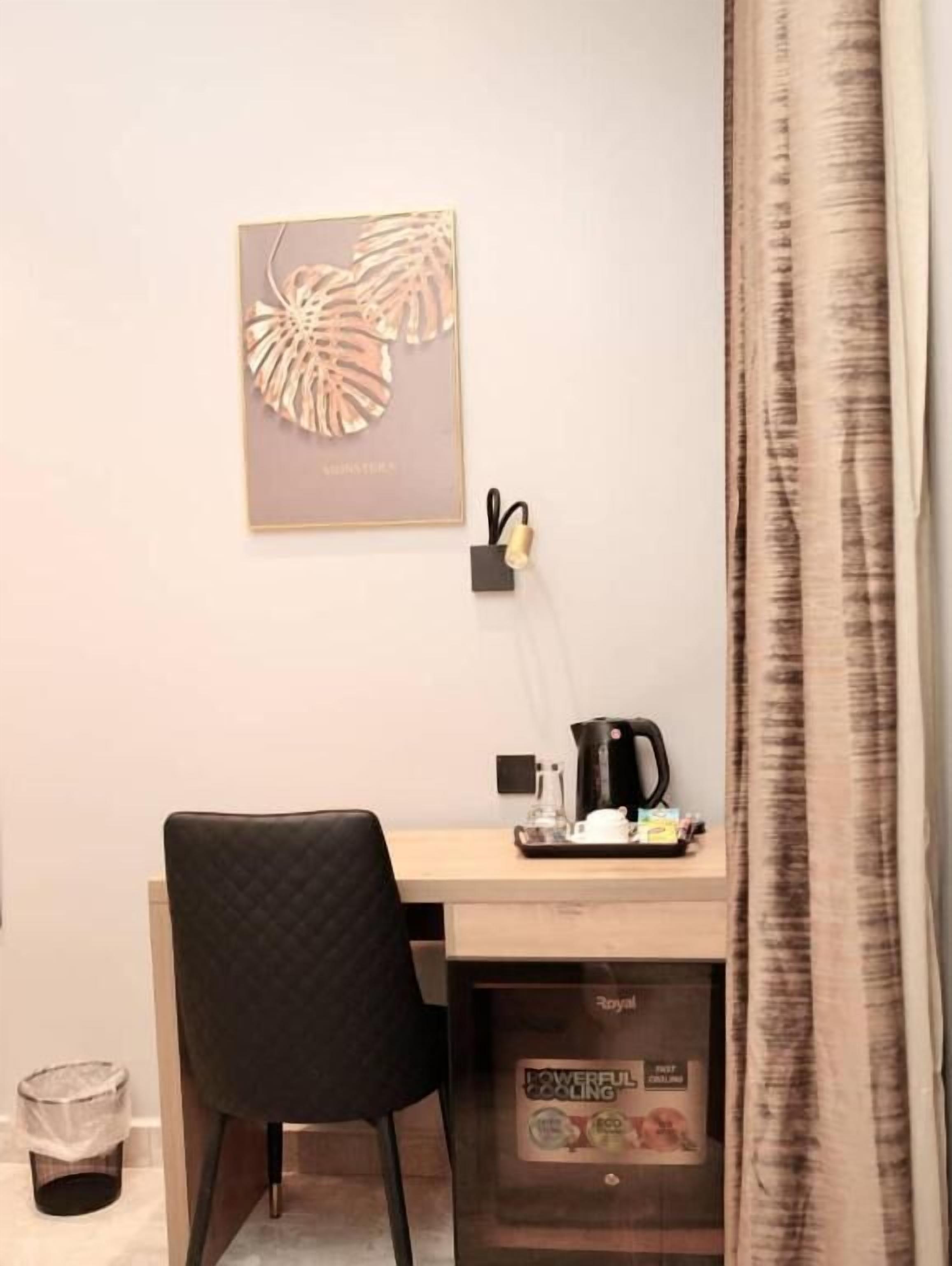 Um quarto pequeno com uma mesa, cadeira e uma obra de arte emoldurada na parede.