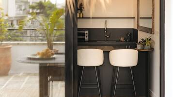 Uma cozinha moderna com bancada preta, dois banquetas brancas, luminária pendente e vista para a rua.