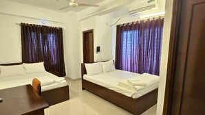 Quarto de hotel com duas camas, uma escrivaninha, um ventilador de teto e um aparelho de ar condicionado.