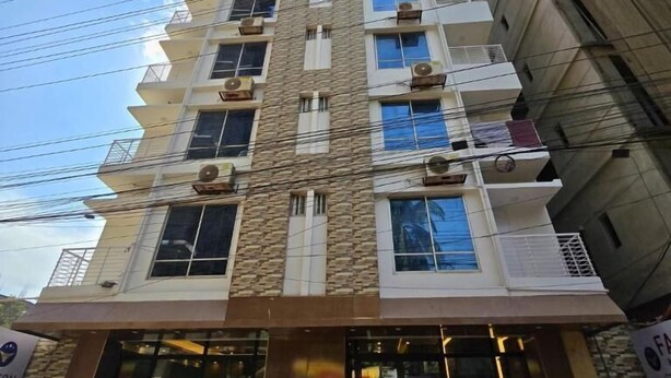 Um edifício com vários andares, entrada central, varandas e aparelhos de ar condicionado.