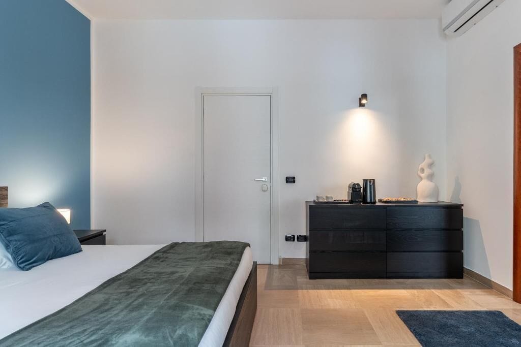 Quarto com cama, cômoda, mesa de cabeceira e porta.