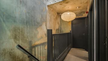 Uma escadaria com corrimão de metal, parede texturizada e luminária suspensa.