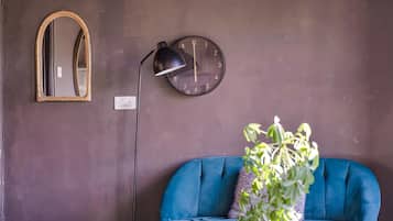 Um quarto com um sofá azul, um relógio de parede, um espelho e um abajur.