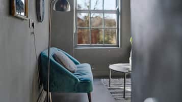 Um quarto com um sofá verde-água, uma mesa redonda, um abajur e uma janela com vista para árvores.