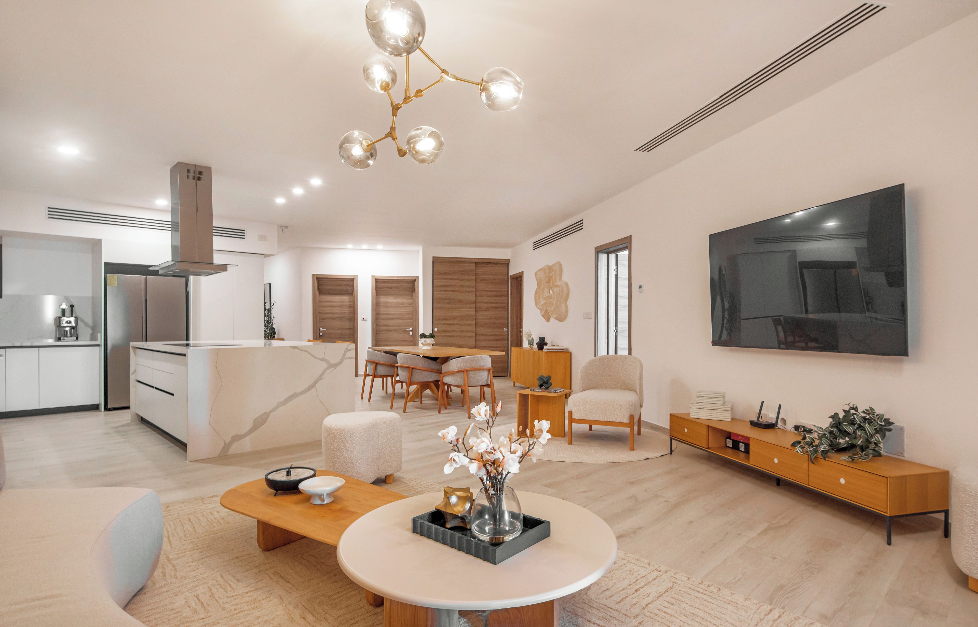 Uma sala de estar moderna com área de jantar, cozinha e uma televisão grande fixada na parede.