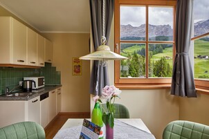 Cozinha com vista para montanhas, mesa de jantar com um vaso de flores e janela com cortinas.