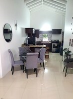 Uma cozinha moderna com armários escuros, uma ilha central e uma área de refeições com cadeiras cinzas.