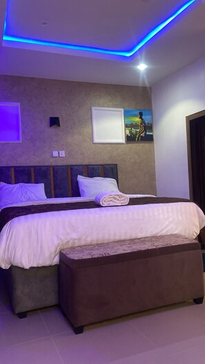 Quarto moderno com cama de casal, um banco e televisão fixada na parede.