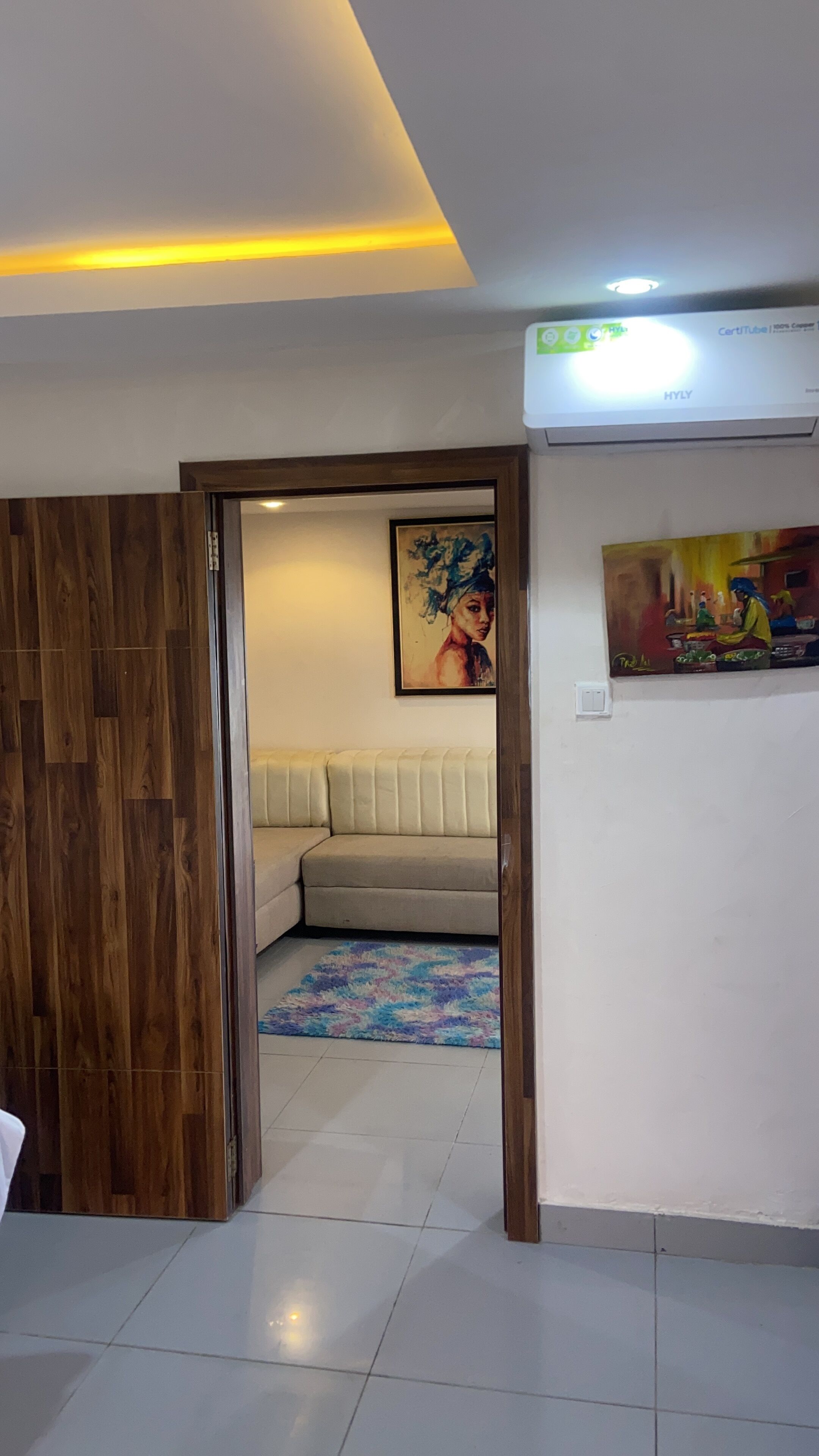 Um espaço interior com porta de madeira, um sofá bege, um tapete colorido e um quadro na parede.
