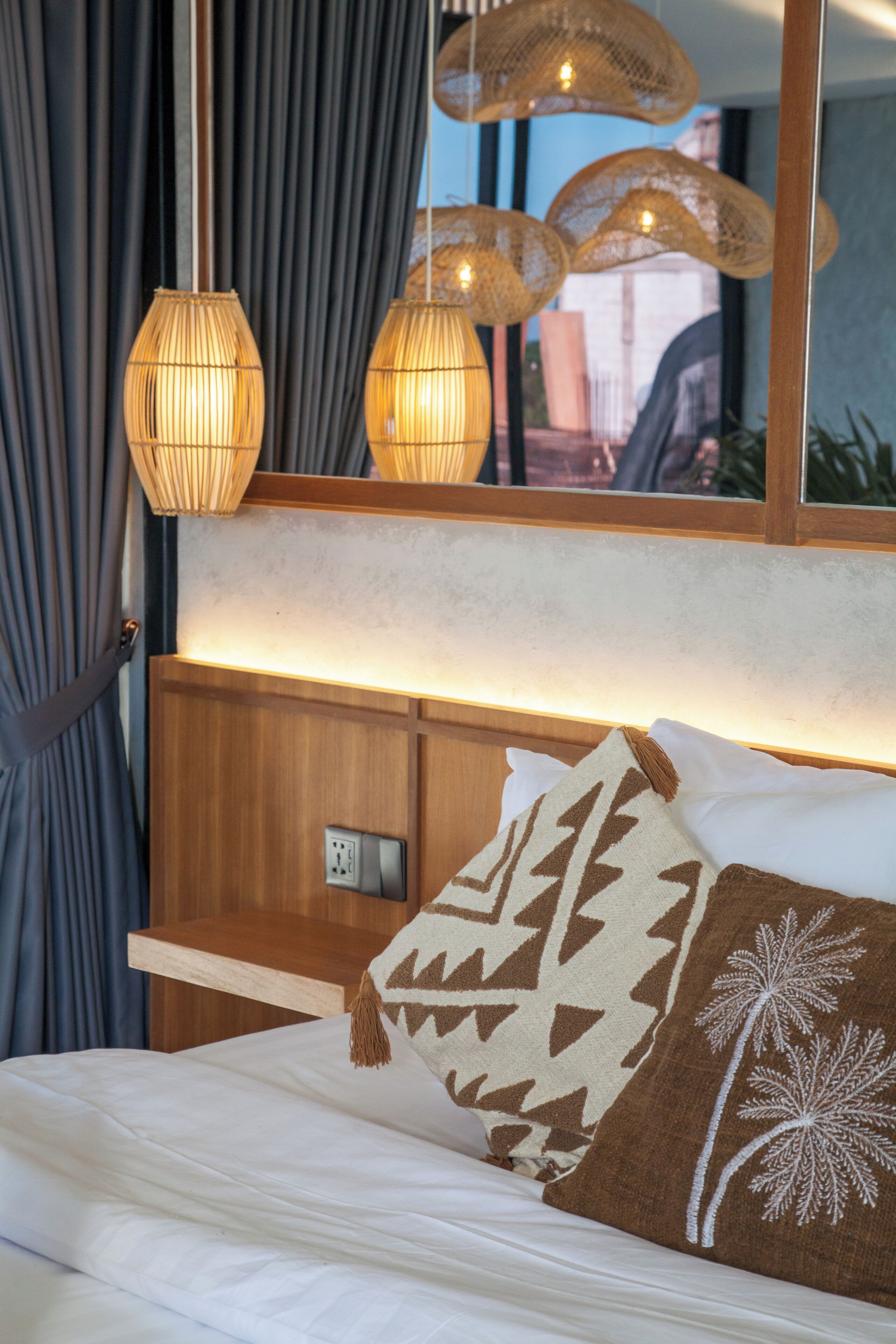 Quarto de hotel com uma cama, cabeceira de madeira, espelho e janela com cortinas.