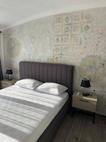 Quarto com uma cama, duas mesas de cabeceira, um criado-mudo, parede estampada e um ventilador de teto.