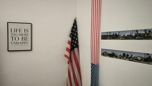 Uma parede com uma moldura de frase, uma bandeira americana e uma faixa vertical com várias fotos.