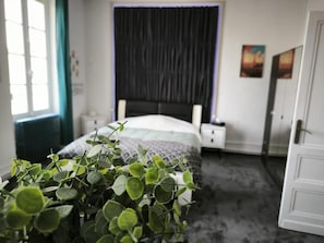 Um quarto com uma cama, mesas de cabeceira, uma janela com cortinas e uma porta.