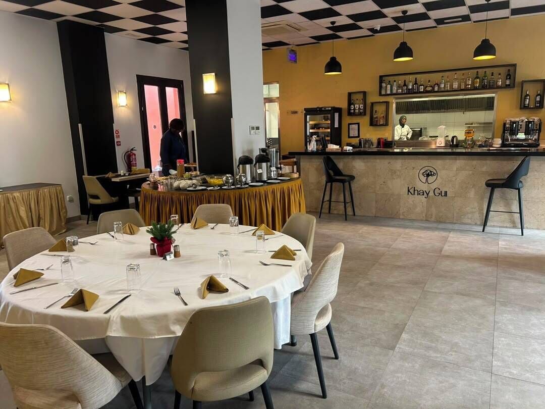 A restaurant with a checkered ceiling, a bar area with Khay Gu branding, and a round dining table set for four.