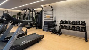 Uma academia com esteiras, equipamentos de musculação e um suporte com halteres.